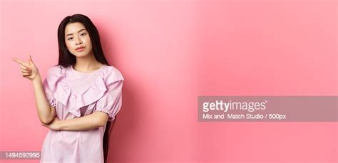 Young Smug Asian Girl Looking Cool And Pointing Finger Left At Logo