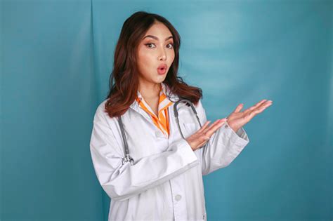 젊은 아시아 여성 의사 의료 전문가의 초상화는 충격을 받고 파란색 배경 위에 격리된 복사 공간을 가리키고 있다 25 29세에 대한 스톡 사진 및 기타 이미지 Istock