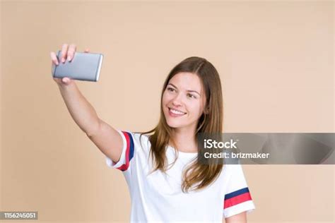 젊은 미소와 아름다운 여자 와 스마트 폰 손에 셀카를 복용 복사 공간 파스텔 베이지 배경에 서 베이지에 대한 스톡 사진 및 기타 이미지 Istock