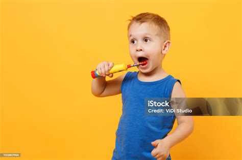 파란 셔츠에 있는 아이 소년 34 세는 밝은 노란 주황색 벽 배경 아이 들 스튜디오 초상화에 고립 된 칫 솔을 가진 그의 이빨을 닦 습니다 사람들 어린 시절 라이프 스타일