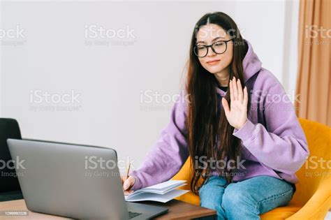 젊은 백인 여성 대학생은 책으로 공부하는 안경을 쓰고 집에서 멀리 떨어진 집에서 화상 통화를 사용하여 직조합니다 먼 교육 개념