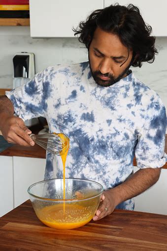 부엌 환경에서 인도 남자의 클로즈업 이미지 나무 부엌 카운터에 유리 믹싱 그릇 계란과 설탕을 섞기 위해 스테인레스 스틸 풍선 거품기를 사용하여 거품기에서 떨어지는 구타 계란