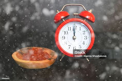올리브 나무로 만든 작은 나무 접시에 빨간 연어 캐비어와 검은 배경에 배치 된 오후 11시 59분에 시간과 함께 둥근 빨간색 클래식 알람 시계 떨어지는 눈 눈 냉동상태의