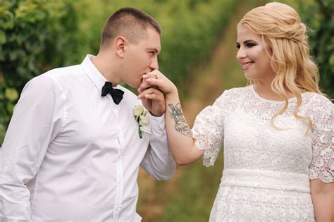 신랑과 신부는 결혼식 날에 포도원에서 걷고 있습니다 금발의 머리 여자는 흰색 드레스에 손에 결혼식 꽃다발을 개최 신랑 키스 신부의 손 로맨스에 대한 스톡 사진 및 기타