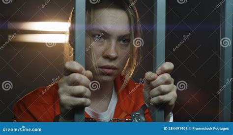 Female Prisoner Stands In Prison Cell Holds Metal Bars By Hands Stock