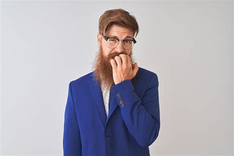 젊은 빨간 머리 아일랜드어 사업가 는 입물고 손톱에 손을 긴장 찾고 고립 된 흰색 배경 위에 양복과 안경을 착용 불안 문제