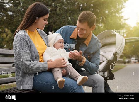 Happy Parents With Their Adorable Baby Sitting On Bench In Park Stock