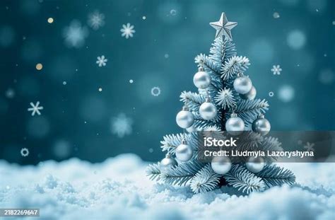 흰색과 파란색 장난감이 있는 은색의 아름다운 크리스마스 트리가 하얗게 반짝이는 눈 위에 서 있고 주변에는 많은 눈송이가 있습니다 0명에 대한 스톡 사진 및 기타 이미지