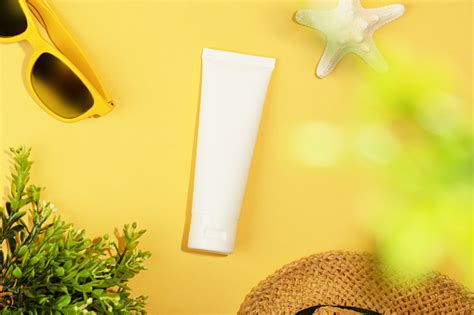 선글라스 불가사리 밀짚 모자 녹색 식물이 있는 여름 배경 노란색 배경에 고립 된 중앙에 브랜드가없는 튜브의 최고 보기 자외선 차단제 크림 세럼용 용기 유기농 화장품 메이크업