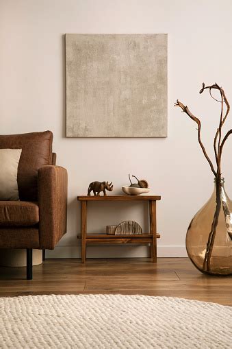 갈색 소파 Pouf 나무 선반 책 모형 포스터 프레임 장식 브런치 및 개인 액세서리가있는 유리 꽃병이있는 세련되고 우아한 객실의 인테리어 디자인 따뜻한 가정 장식 템플렛 0