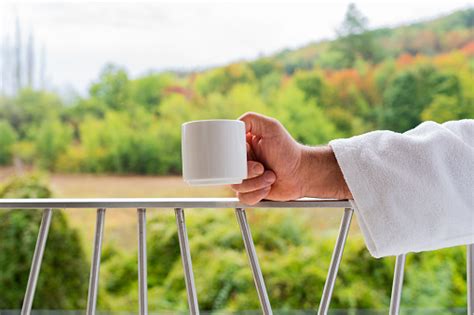 목욕 가운을 입은 남자가 스파 호텔의 테라스에서 커피를 들고 있는 모습 그가 머무는 곳 배경에 아름다운 자연을 배경으로 한 남자의 손 클로즈업 Brand Name Smart