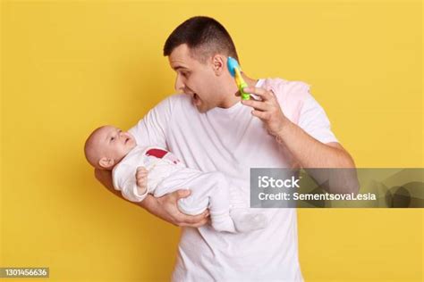 딸랑이 장난감을 들고 놀고 노란 배경위에 고립 된 아기를 진정시키고 아빠가 노래를 부르거나 손에 들고 아이를 위해 무언가를