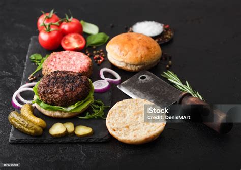 검은 바탕에 빵 양파와 토마토를 곁들인 돌 도마위에 신선한 구운 생 다진 후추 소고기 버거 고기 도끼와 짠 피클과 바질 텍스트를