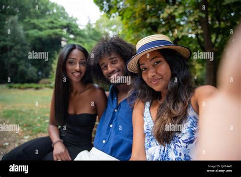 Portrait Of Three Smiling Friends Sitting On A Bench Taking A Selfie In