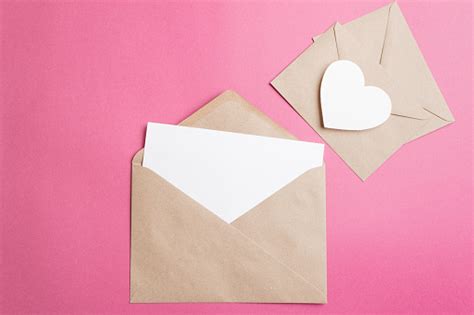 발렌타인 데이에 대한 낭만적 인 사랑 편지의 개념 커프 페이퍼로 만든 열린 봉투에 빈 종이가 있고 분홍색 배경에 하얀 하트가