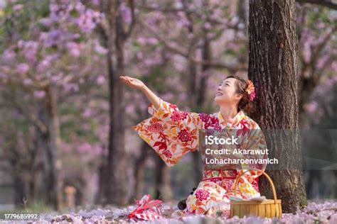 전통 기모노 드레스를 입은 일본 여성이 봄 벚꽃 축제 기간 동안 벚꽃 나무의 공원에 앉아 달콤한 하나미 경단 디저트를 들고