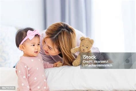 아시아인 어머니는 가족의 행복과 육아 사용을 위해 침대에서 좋은 시간을 보내면서 예쁜 웃는 아기 딸을 안고 있습니다 12 17