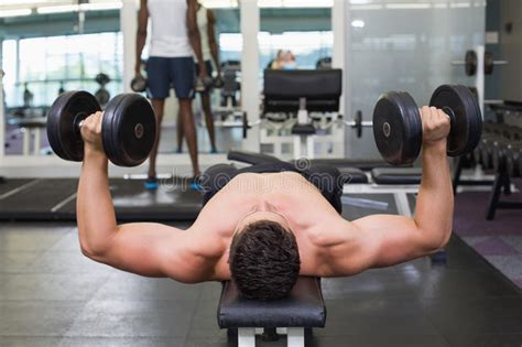 Без рубашки культурист лежа на стенде поднимая тяжелые гантели Стоковое Изображение