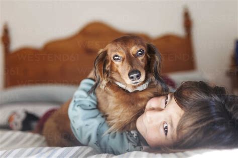 Lächelnder kleiner Junge liegt mit langhaarigem Dackel auf dem Bett lizenzfreies Stockfoto