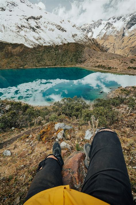 검은 바지와 갈색 하이킹 신발을 신은 사람이 낮에 호수 근처의 바위에 앉아 있다 사진 Unsplash의 무료 라구나 휴먼타이 이미지