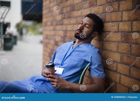 Tired Caregiver Man Resting Outdoor In Front Of Nurishing Home Stock