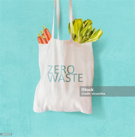 밝은 파란색 배경 앞에 매달려있는 야채로 가득 찬 제로 폐기물이라는 비문이 새겨진 흰색 천 가방 0명에 대한 스톡 사진 및 기타
