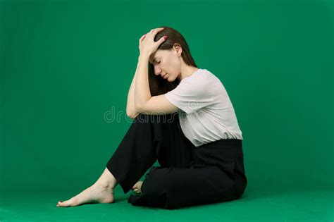 A Young Woman Sits On A Green Background Holds Her Head With Her Hands