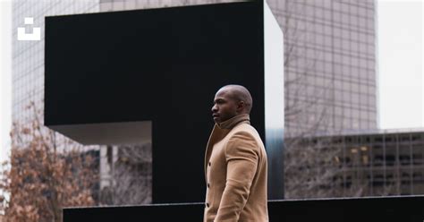 갈색 코트를 입은 남자가 낮에 검은 기념비 근처를 걷고 있다 사진 Unsplash의 무료 시티가든 이미지