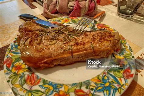 큰 쇠고기 스테이크를 요리 하 고 로즈마리와 함께 양념 여전히 접시에 흡연 나이프와 포크는 슬라이스 할 준비가 되어 있습니다 백그라운드에서 테이블이 설정 됩니다 고기에 대한