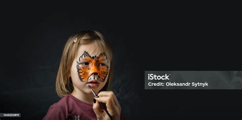 검은 배경에 호랑이 얼굴 그림을 그린 귀여운 백인 소녀 얼굴 페인팅으로 어린 아이의 초상화를 닫습니다 호랑이의 해 그녀가 호랑이