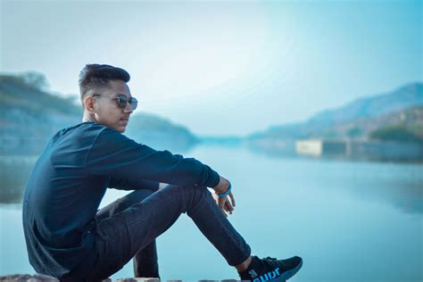Man In Black Long Sleeve Shirt And Blue Denim Jeans Sitting On Rock