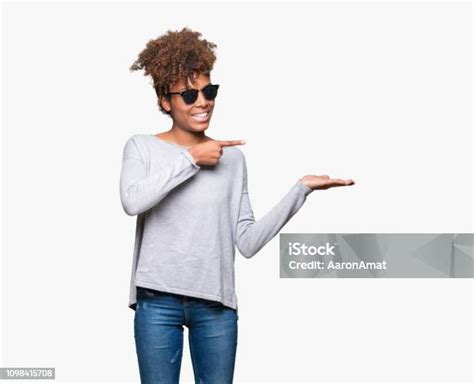 美麗的年輕非洲裔美國婦女戴著太陽鏡在孤立的背景驚訝和微笑的相機 而提出的手和手指指指點點 照片檔及更多 一個人 照片 一個人 人 人手