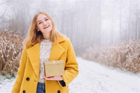 자연 배경 위에 크리스마스 선물 상자를 들고 코트를 입고 행복한 젊은 여성 2021 년 의 트렌디 한 색상 노란색 조명 휴일 컨셉 2021년에 대한 스톡 사진 및 기타