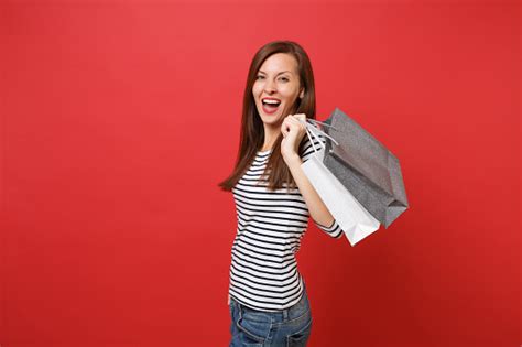 붉은 벽 배경에 고립 쇼핑 후 구매와 패키지 가방을 들고 줄무늬 옷에 쾌활 한 젊은 여자의 초상화 사람들이 진심으 감정 라이프 스타일 개념 복사 공간을 비웃는 다 갈색
