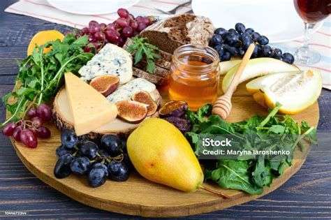 다양 한 전채 포도 치즈 블루 치즈 무화과 멜론 Arugula 곡물 빵 꿀 나무 테이블에 둥근 나무 쟁반에 과일에 대한 스톡