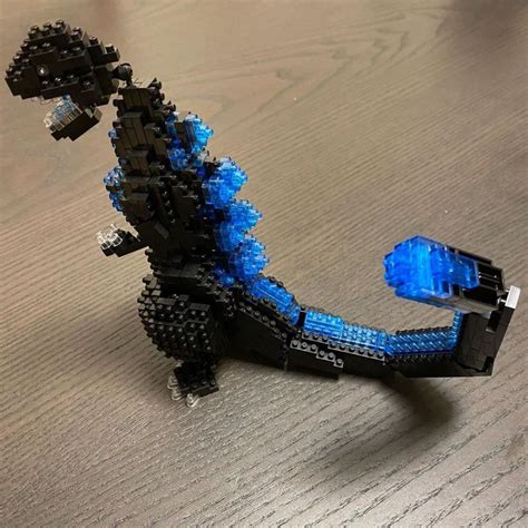 A Lego Godzilla Sitting On Top Of A Wooden Table Next To A Blue Light Bulb
