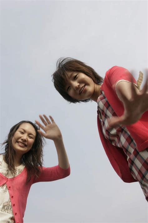 东方人 两个人 伙伴 朋友 站 举 竖图 室外 白天 仰视 友谊 亚洲 弯腰 服装 挥手 注视 休闲装 黄种人 衣服 蓝色 蓝天 天空 天