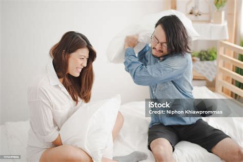 젊은 부부 아시아 남자와 여자 앉아 흰색 침대에 재미 와 벌채 행복 때 베개 싸움 에 침대 방 에 집에서 2명에 대한 스톡 사진