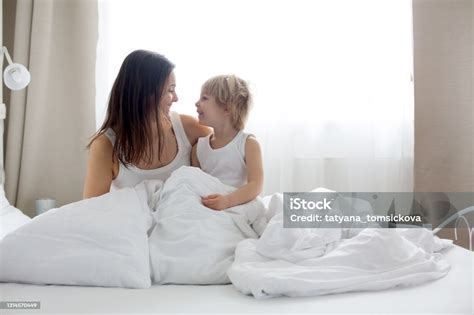 아름다운 금발의 아이와 그의 어머니 침대에서 아침에 집에서 놀고 웃고 웃고 재미있게 지내고 있습니다 2명에 대한 스톡 사진 및