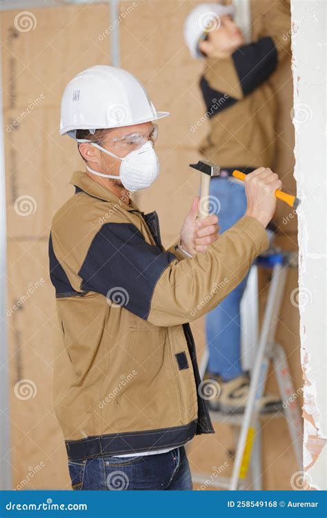 Builders Working Indoors Man In Foreground Using Hammer And Chisel