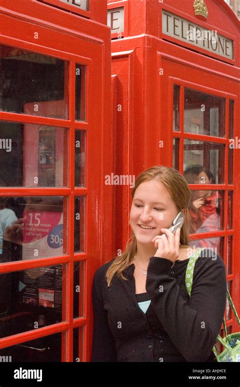 Teenager Using Cell Phone In Front Of Traditional Red Phone Booths In