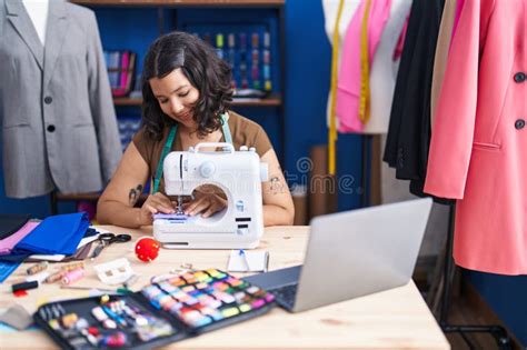 Young Woman Tailor Using Sewing Machine And Laptop At Sewing Studio