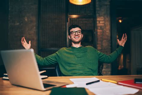 행복한 젊은 정서적 기업가 는 흥분과 작업 과정의 행복은 실내에서 좋은 일을 만들기 넷북과 종이와 바탕 화면에 앉아 안경에 성공적인 미소 힙스터 남자 It 전문가에 대한