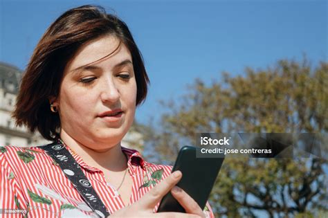 젊은 라틴어 플러스 크기의 여성의 초상화 야외에서 전화로 친구에게 메시지를 보내는 모습 Brand Name Online Messaging Platform에 대한 스톡 사진