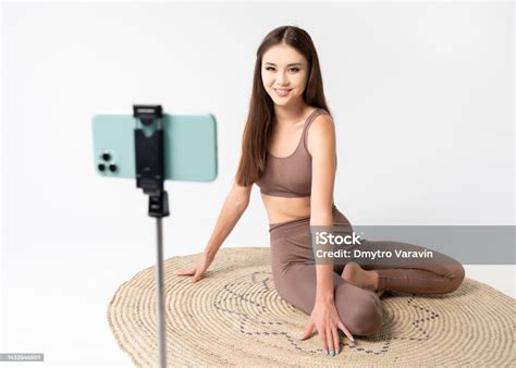 요가 온라인 집에서 온라인 훈련은 삼각대를 들고 핸드폰에 맞서 바닥에 앉아있는 아시아 여성과 함께합니다 18 19세에 대한 스톡