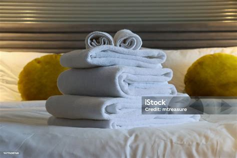 하얀 이불 더블 침대 커버 접힌 목욕 시트와 핸드 타월 질감이 있는 배턴 헤드보드에 하얀 베개 더미에 기대어 있는 원형의 노란색