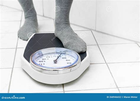 Feet In Socks Stepping On A Personal Scale On The Tiled Bathroom Floor