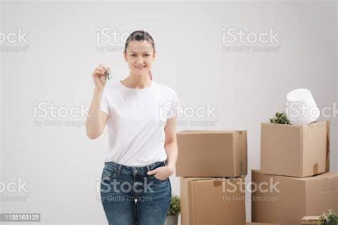 흰색 T 셔츠에 젊은 아름 다운 갈색 머리 소녀는 물건과 판지 상자의 배경에 대해 그녀의 손에 새로운 집에 열쇠를 보유 하 고 있습니다 Fashion Show에 대한 스톡