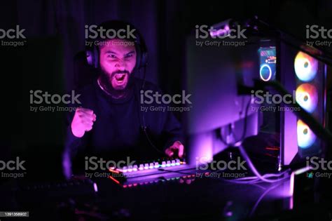 수직 사진 한 젊은이는 여러 가지 색의 네온 조명으로 조명 된 방에서 컴퓨터 게임을합니다 게임 플레이는 재미 있고 만족 스럽습니다 블랙 스튜디오에서 만족감으로 주먹을 들어