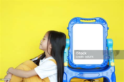 수업 시간에 공부하기 위해 화이트 보드를 들고 있는 아시아의 어린 소녀 빈 화이트보드를 들고 있는 여학생은 노란색 배경에 고립되어 있다 두뇌 발달 개념을 가진 학생 4 5